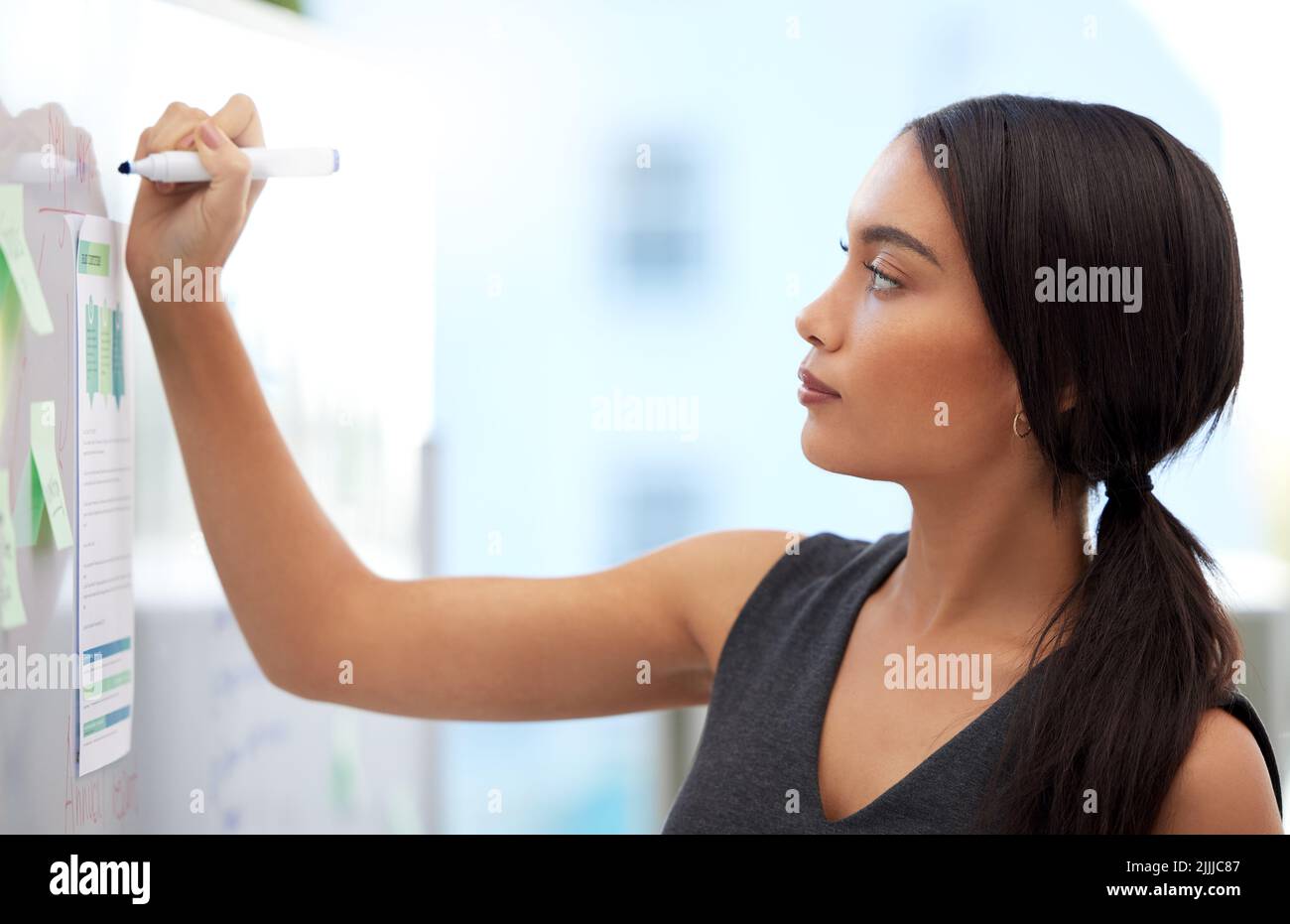 Putting her vision onto the board. a young businesswoman writing notes ...