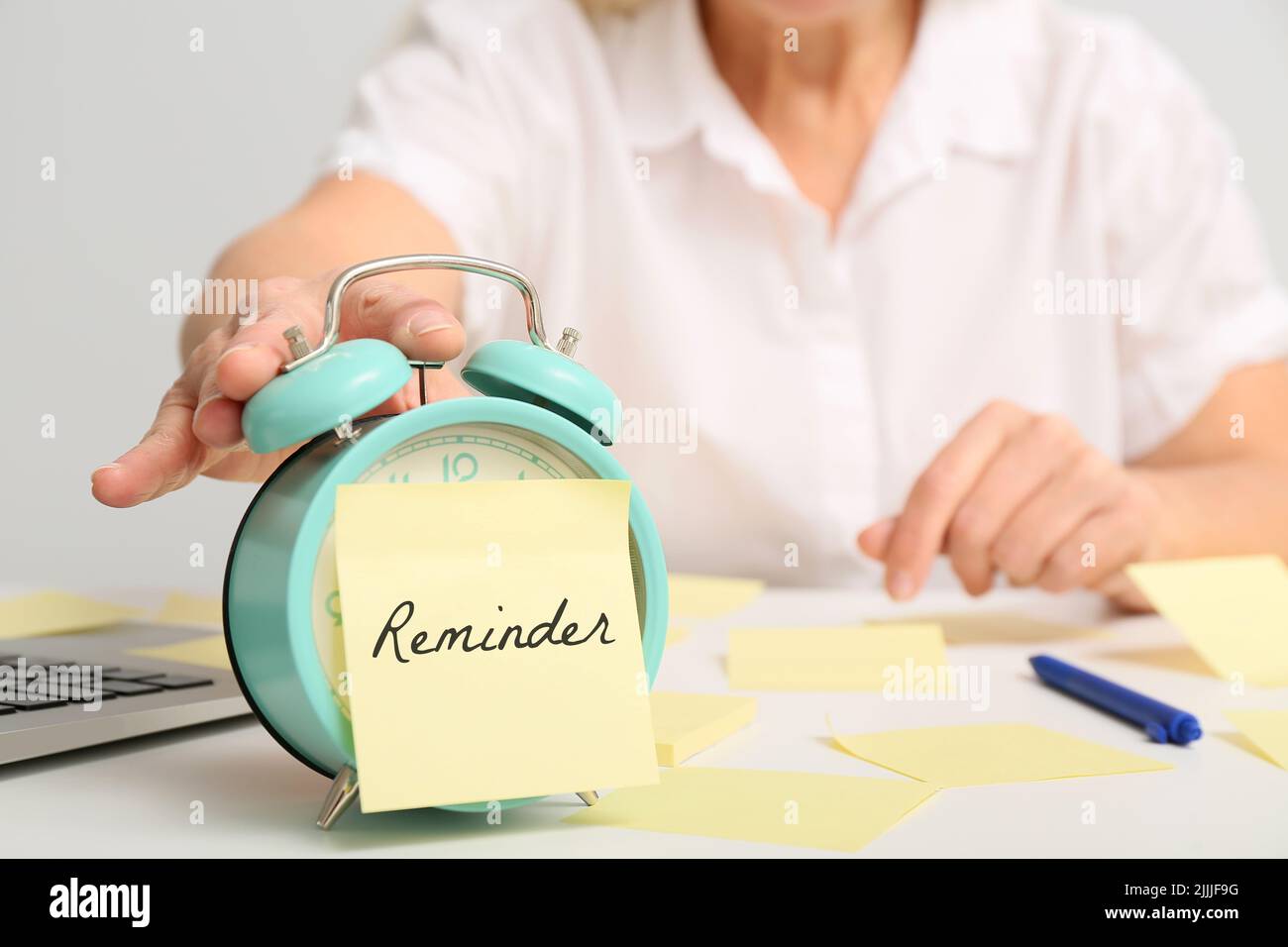 Sticky note paper with word REMINDER on alarm clock at workplace of ...