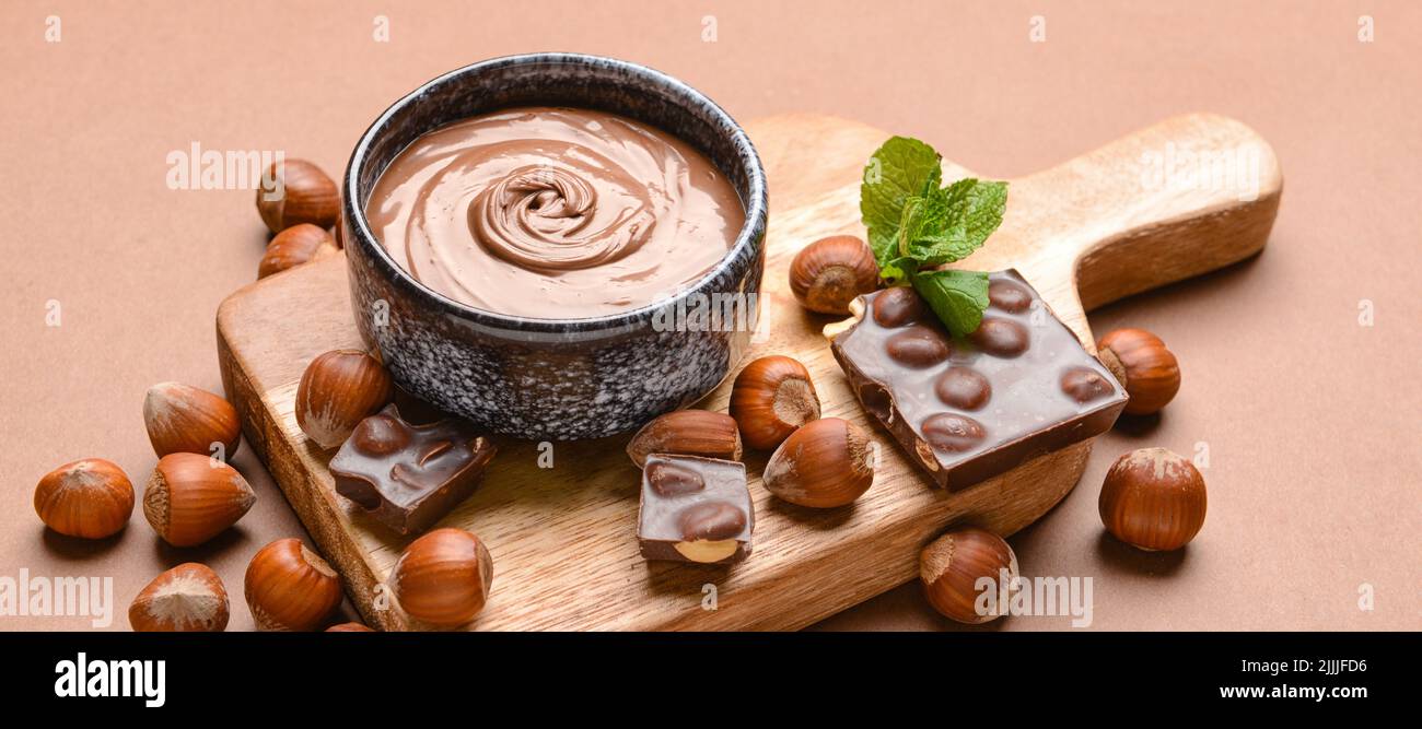 Bowl with tasty chocolate paste and hazelnuts on color background Stock ...