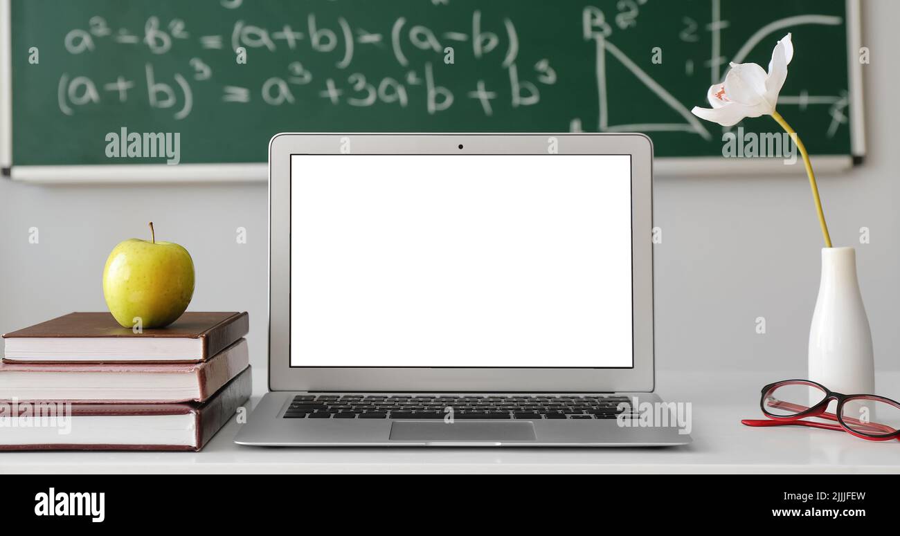 Laptop, books and apple on teacher's table in classroom Stock Photo - Alamy