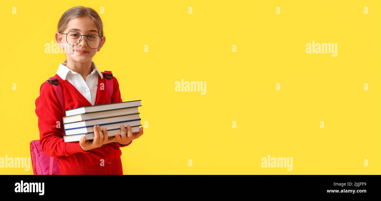 Cute little school girl holding books on yellow background with space ...