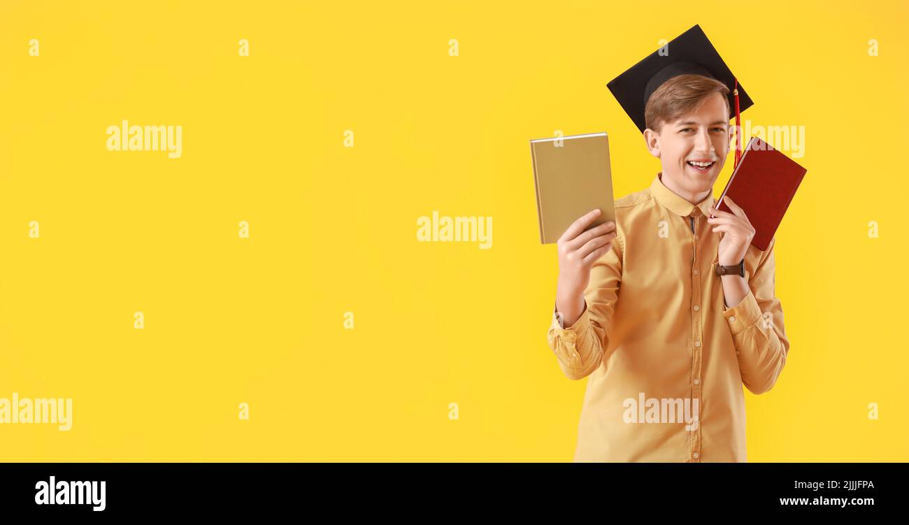 Male graduating student holding books on yellow background with space ...