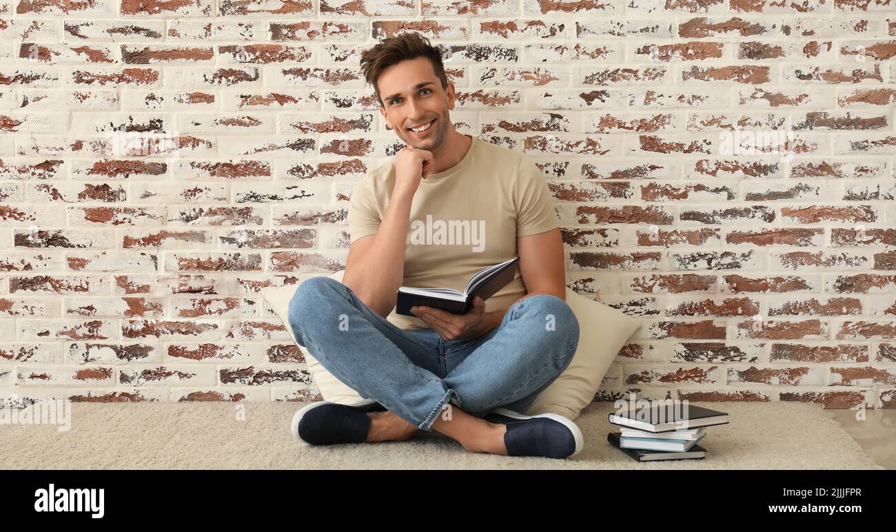 Handsome young man with books sitting near brick wall Stock Photo - Alamy