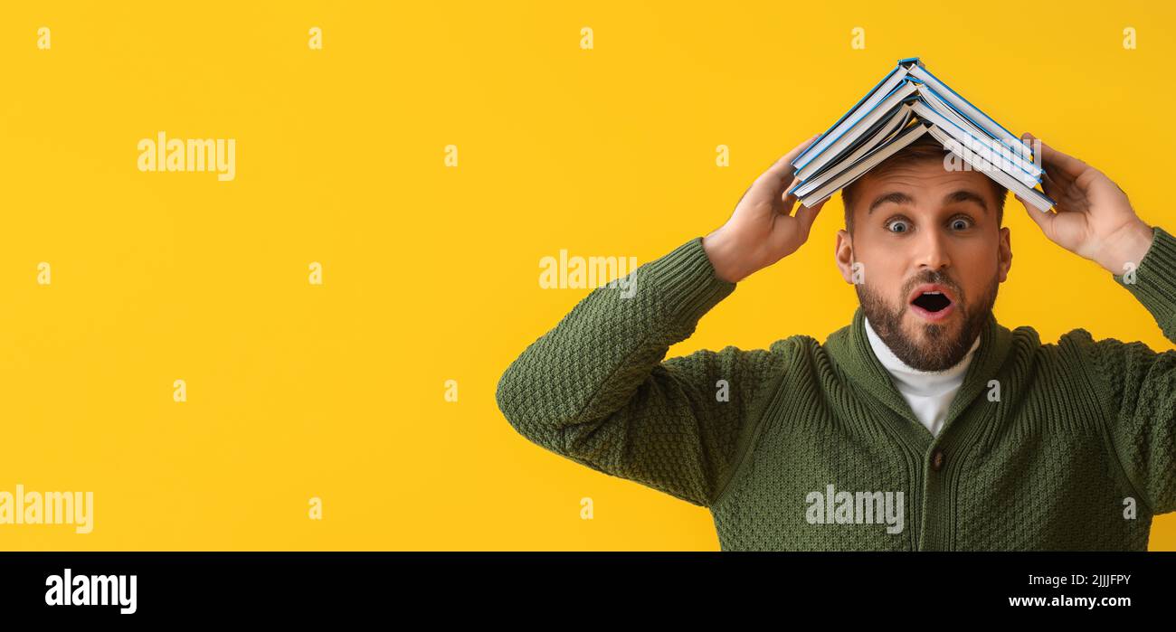 Surprised young man with books on yellow background with space for text ...