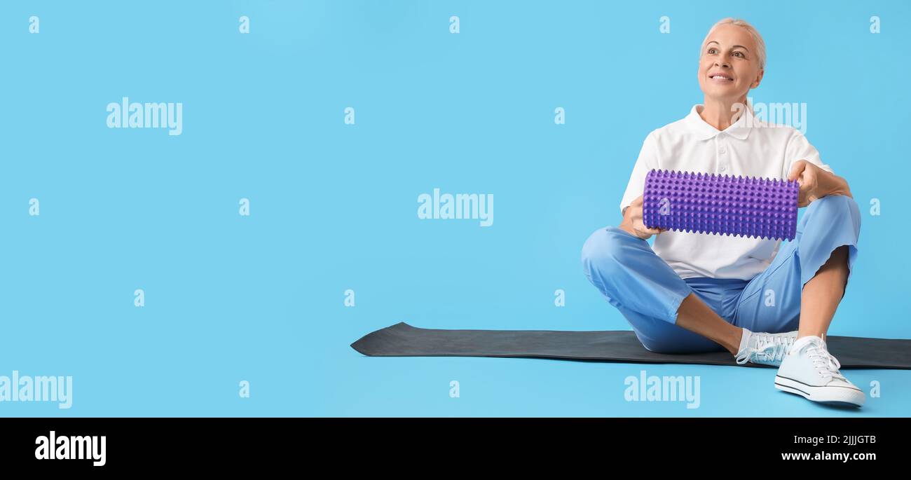 Mature woman holding foam roller on blue background with space for text ...