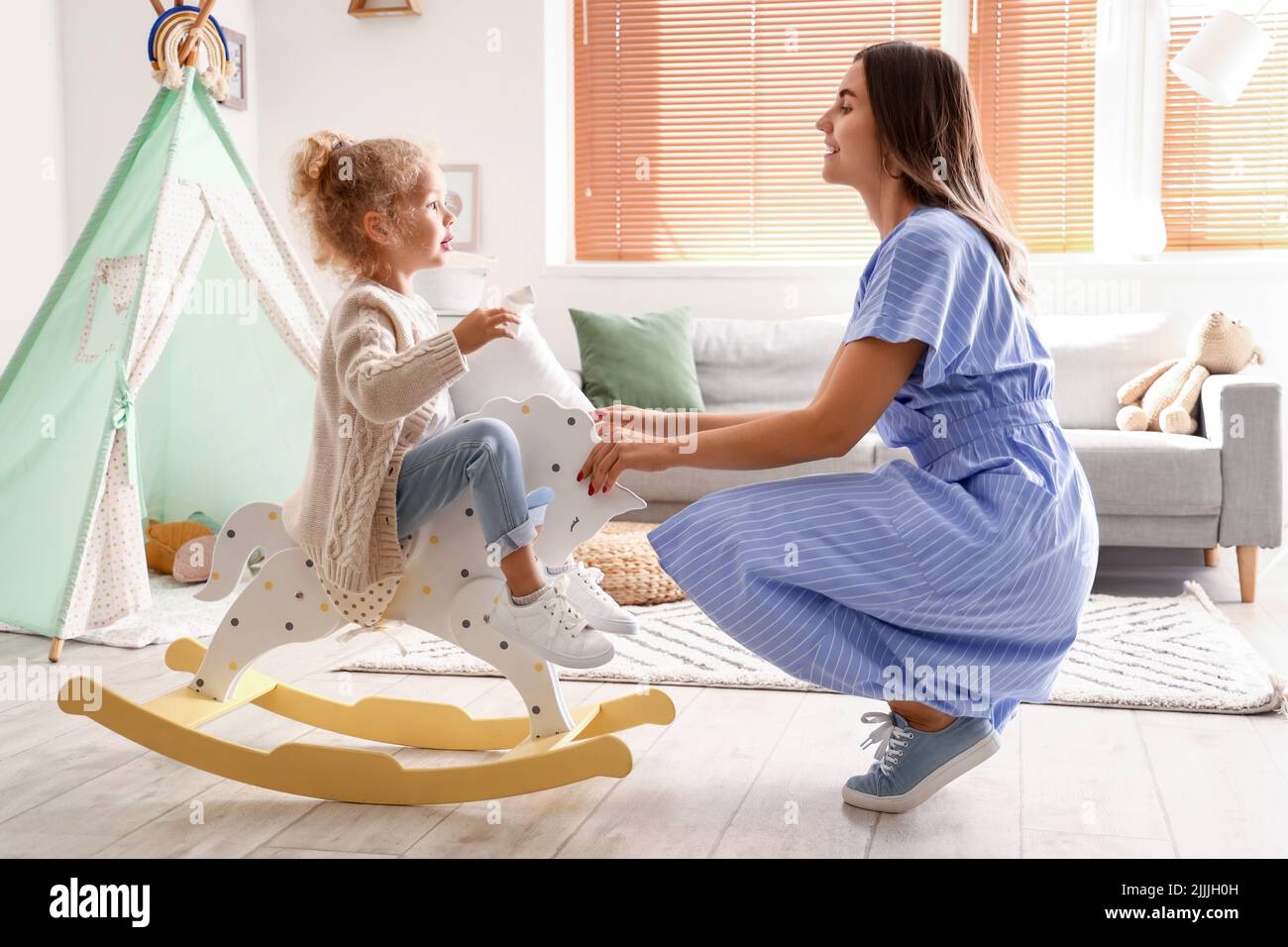 Cute little girl with pillow, rocking horse and her mother at home ...