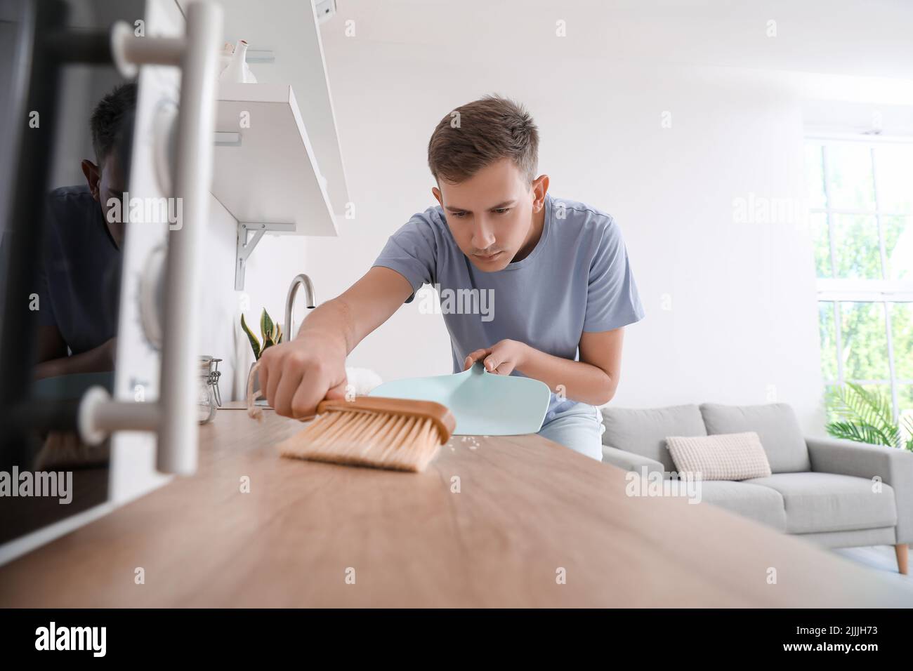 Young man sweeping table top in kitchen Stock Photo - Alamy
