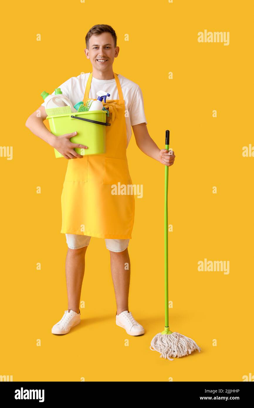 Smiling young man with cleaning supplies on yellow background Stock ...