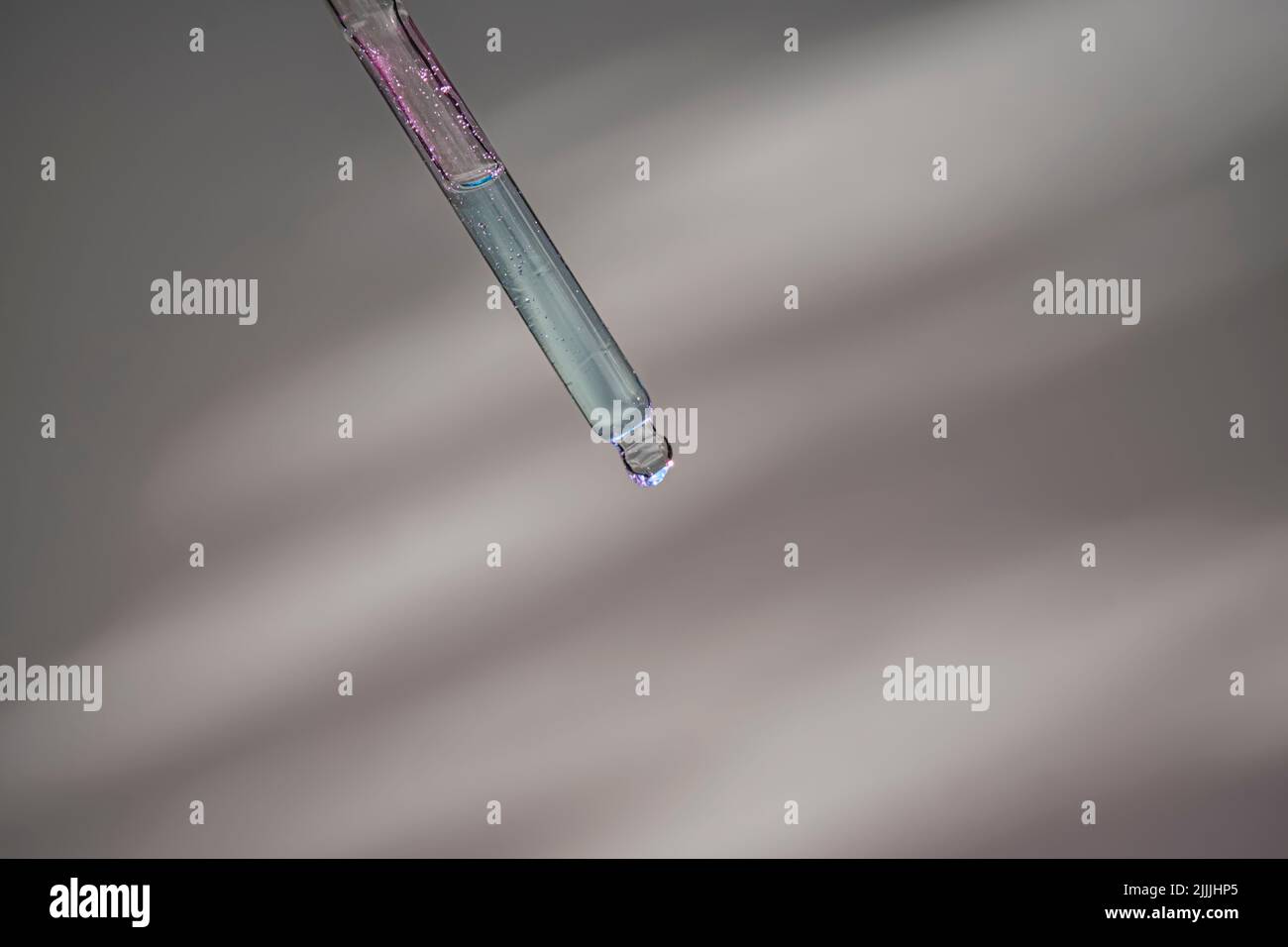 Liquid serum and dropper on a gray background with sun glare. Frontal ...
