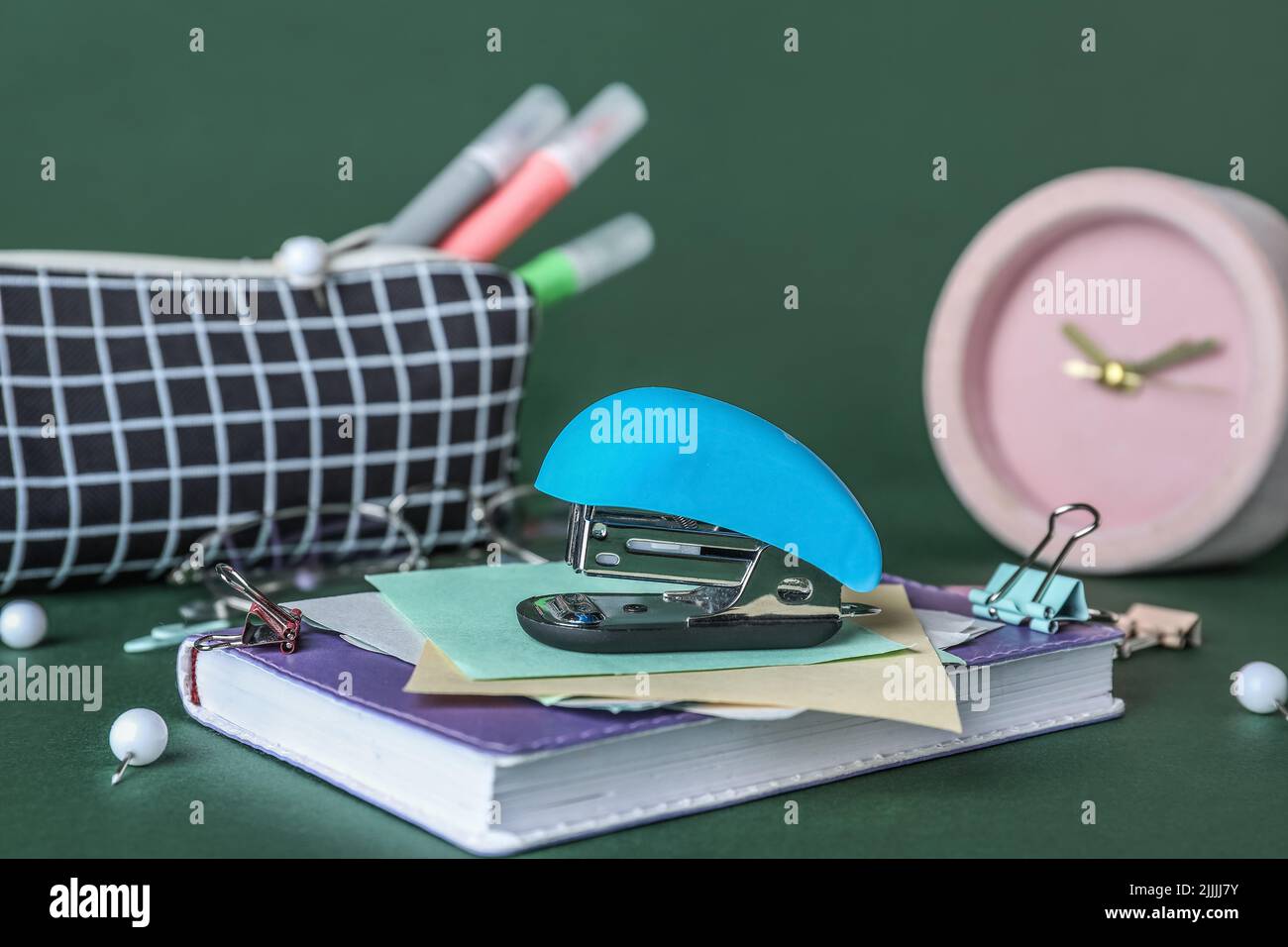 Stapler with different stationery supplies and alarm clock on green ...