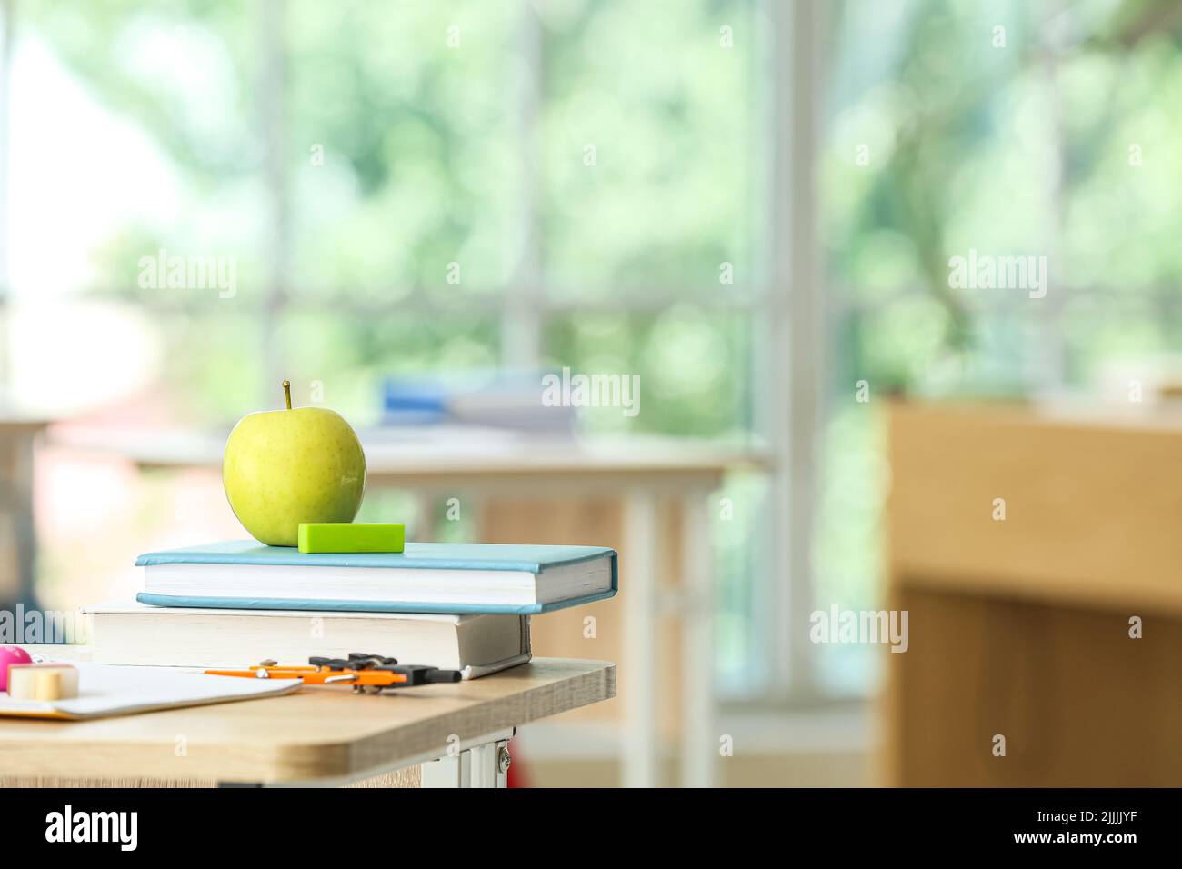 Apple with school books and stationery supplies on table in classroom ...