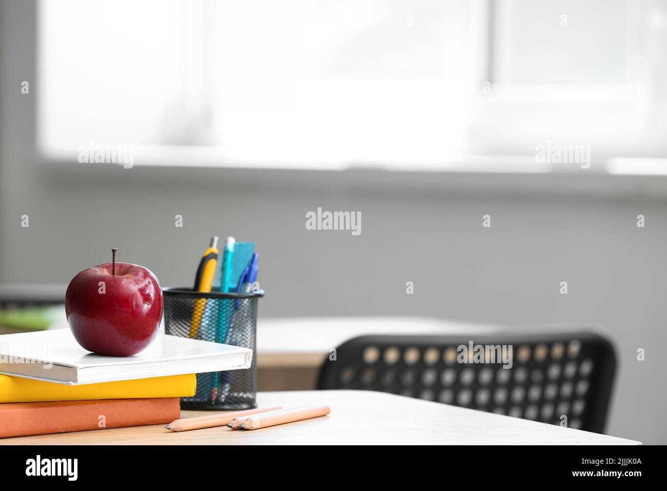 Apple with books, pen cup and school stationery on table in classroom ...