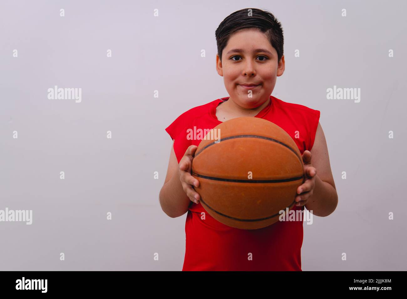 A sporty boy wearing a red basketball jersey holding a ball on an ...