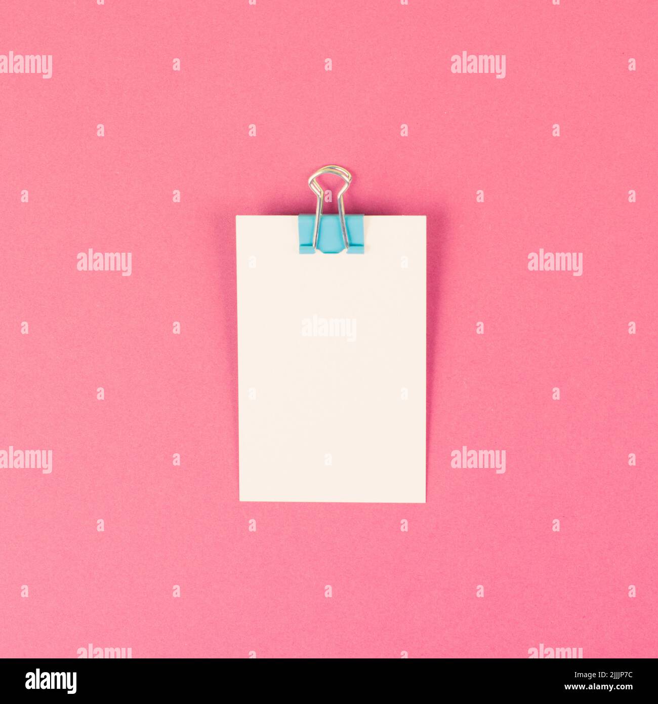 Blank white paper with a paperclip on a pink colored background, copy ...
