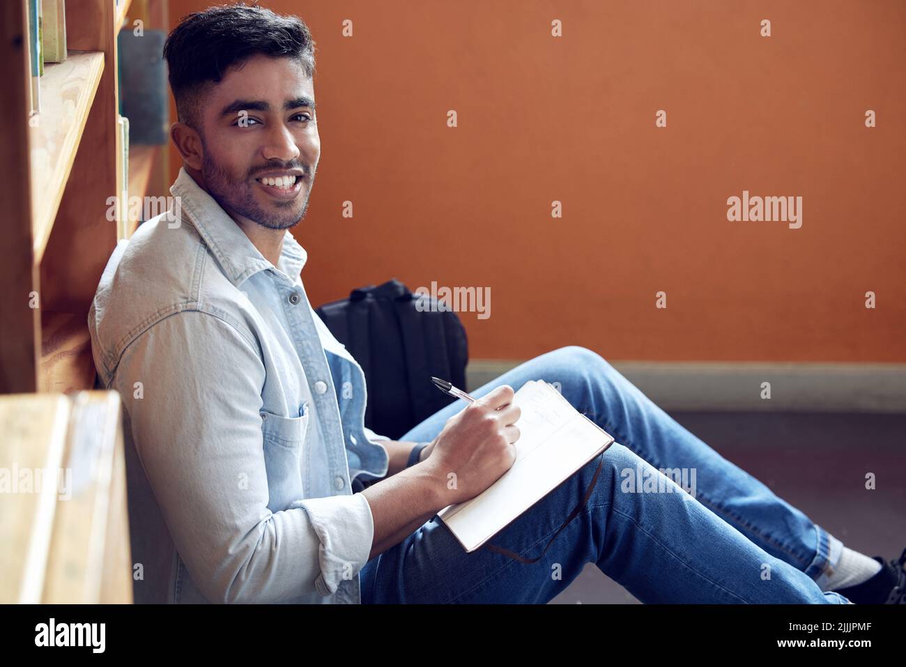 My success story starts here. a young man making notes in a library at ...