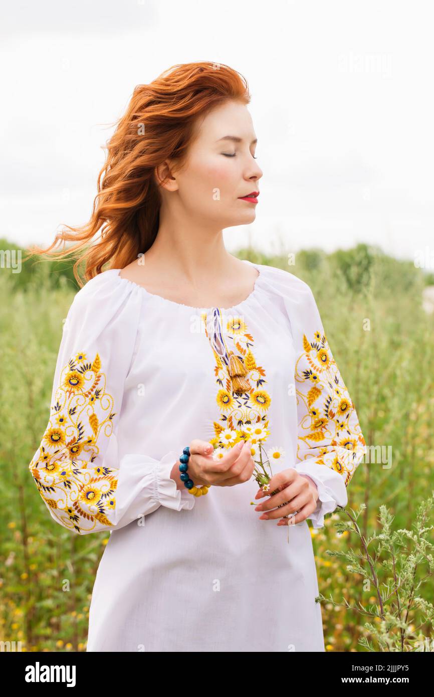 A woman in a Ukrainian folk costume in a field with a bouquet of wild ...