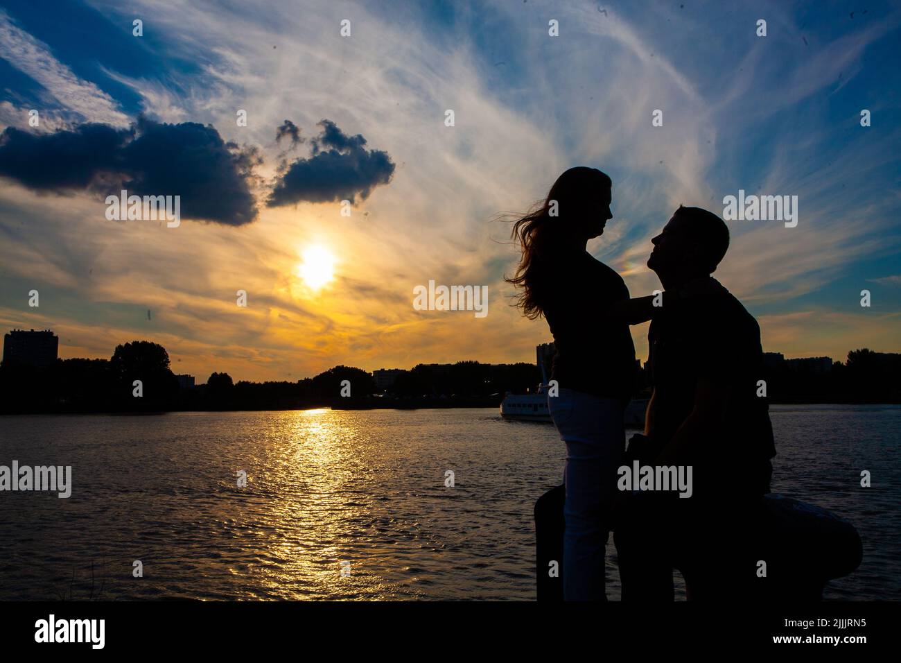 Silhouette of a loving couple cuddling during a golden sunset reflected ...