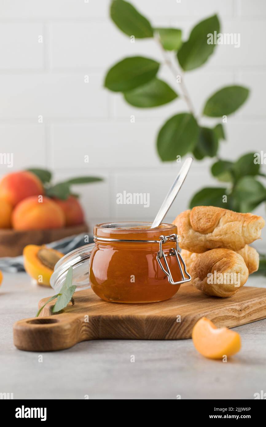 A jar of apricot jam with a spoon inside and with croissants, ripe ...