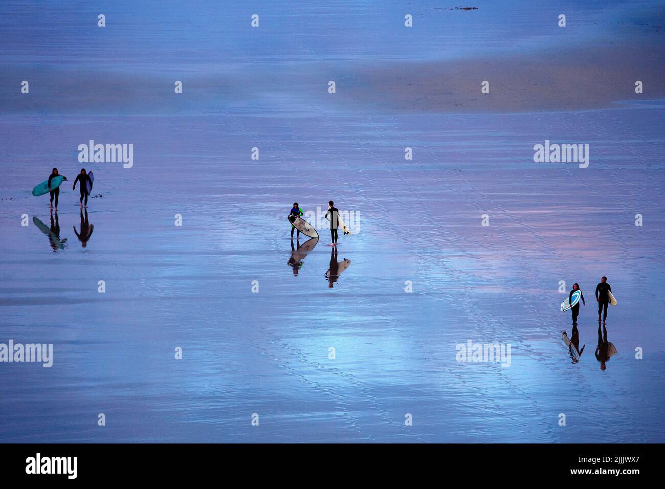 British surfers return home across a beautiful turquoise beach after a ...