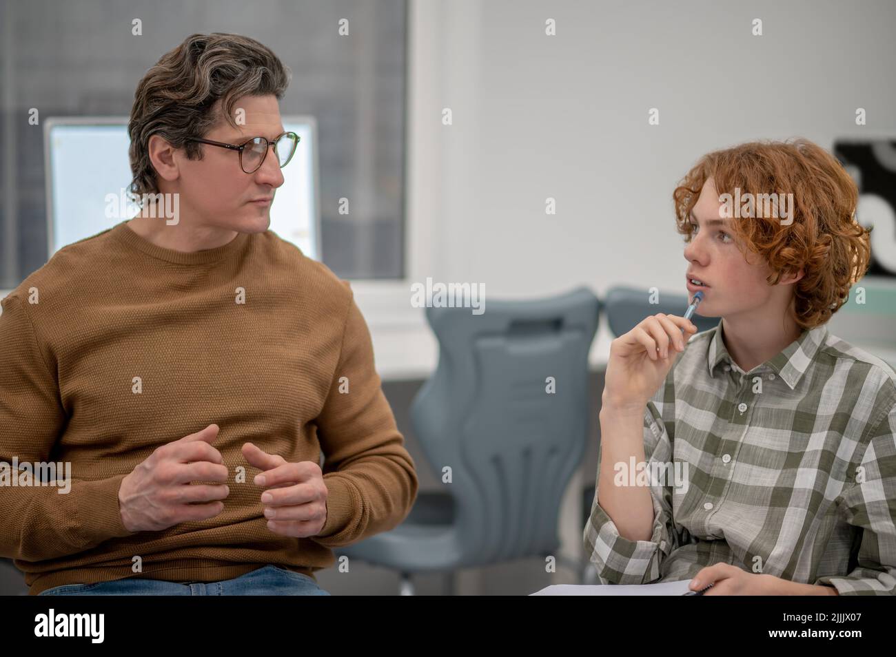Ginger boy sitting next to teacher and looking interested Stock Photo ...