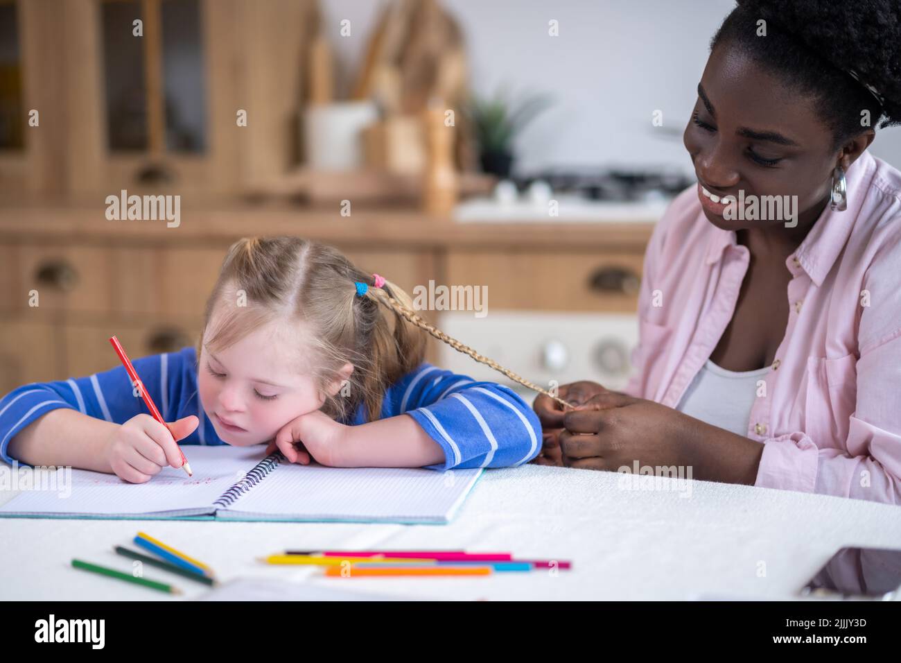 A positive happy woman making braids to a cute girl sitting next to her ...