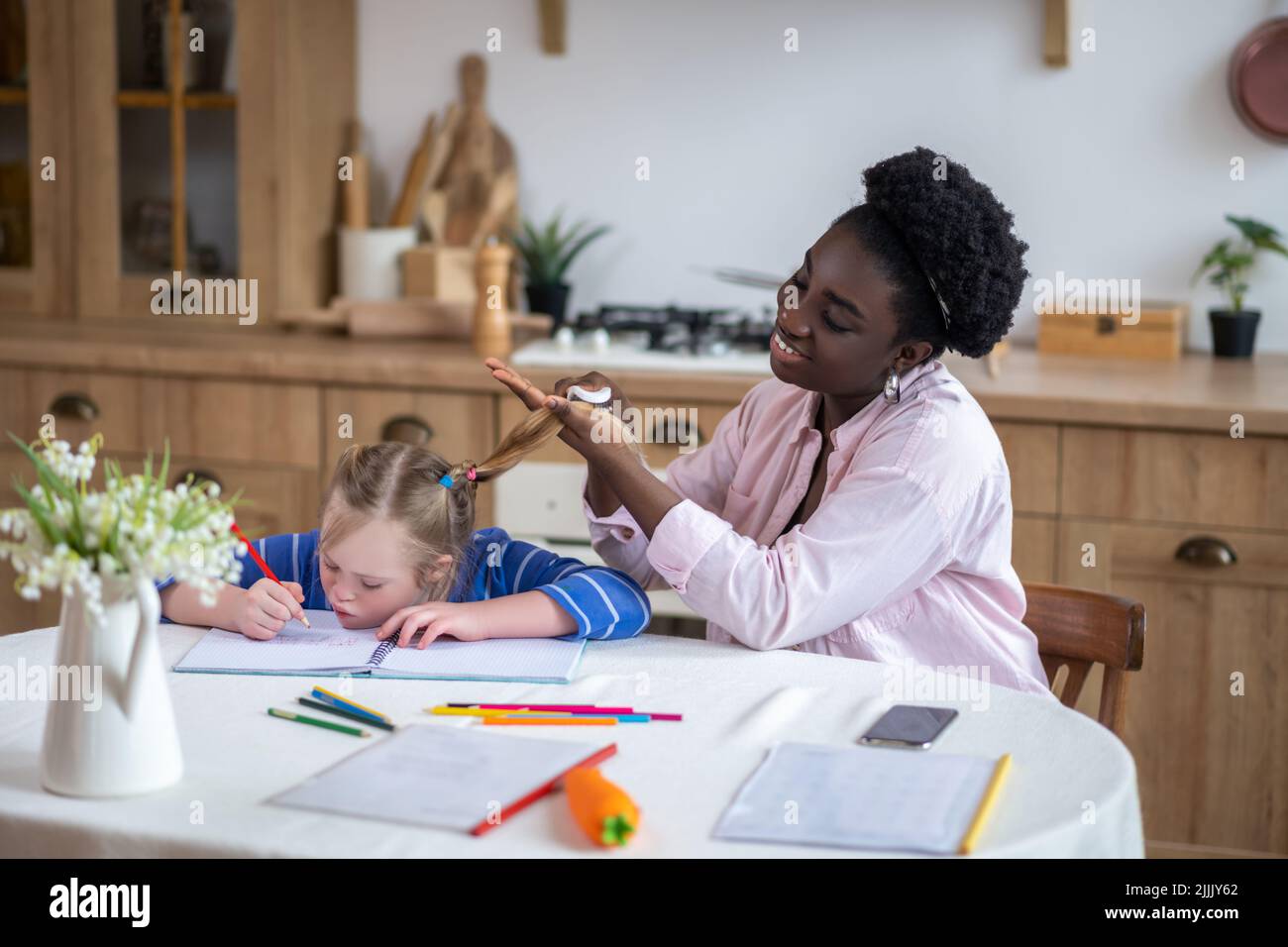 A positive happy woman making braids to a cute girl sitting next to her ...