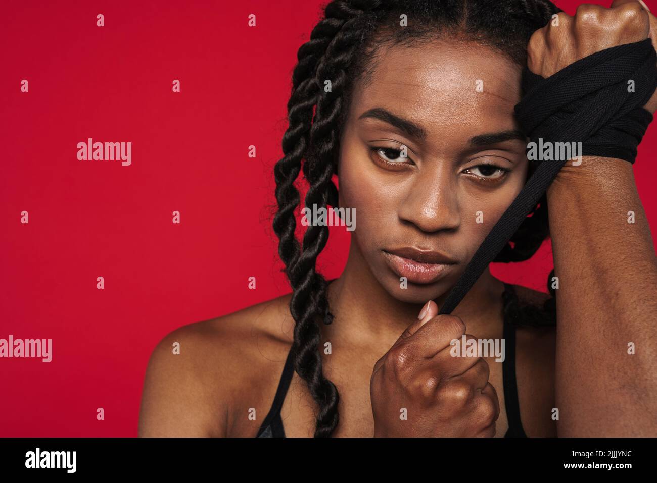 Young black sportswoman wearing bra posing with rope isolated over red ...