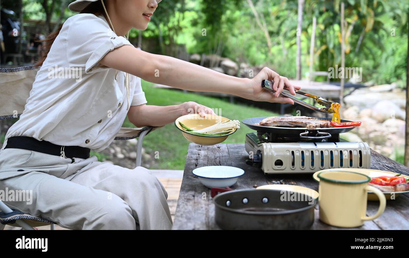 Female traveler siting on folding chair and grilling barbecue during ...