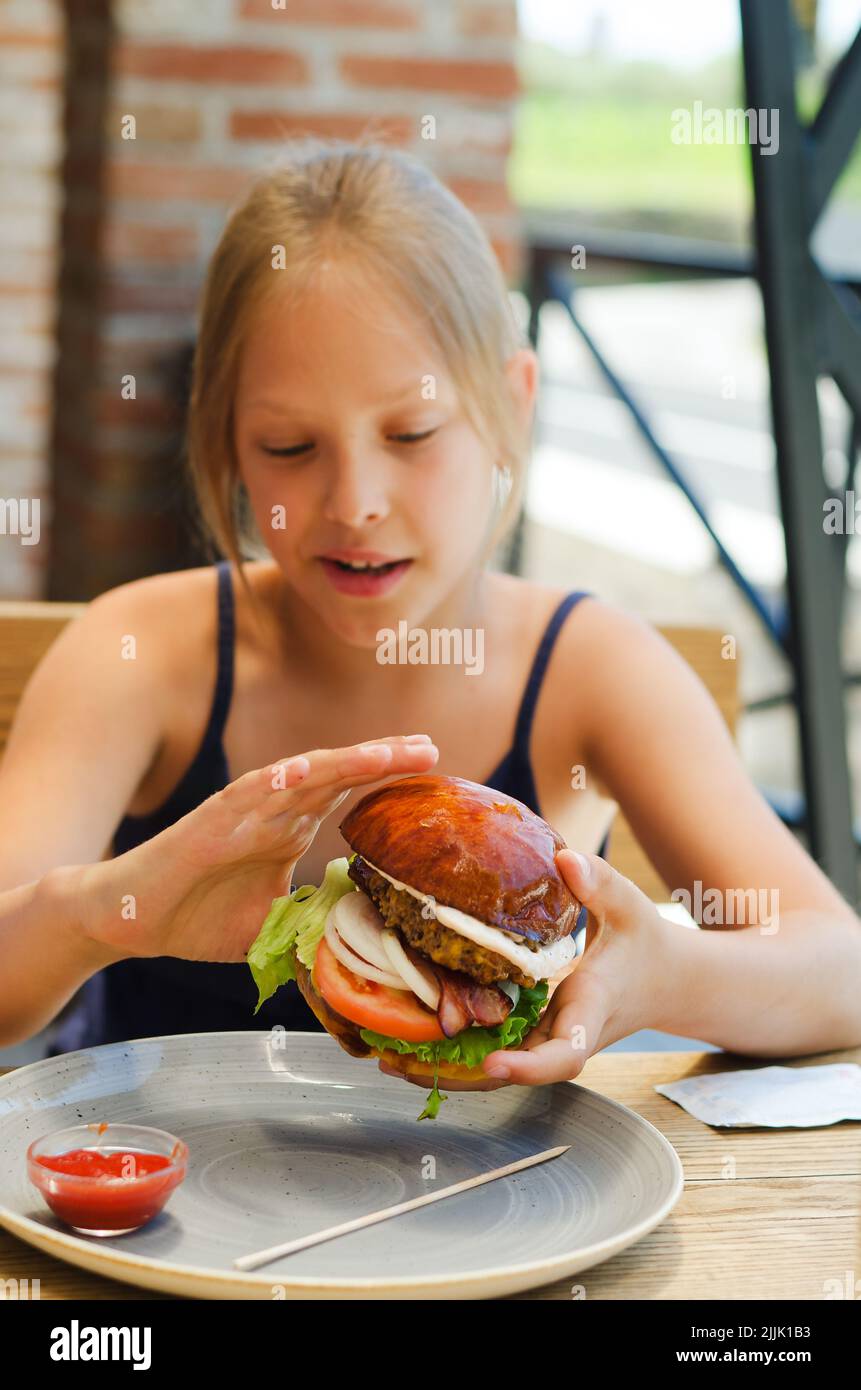 Happy girl, teenager eating a burger with a meat patty in a restaurant ...