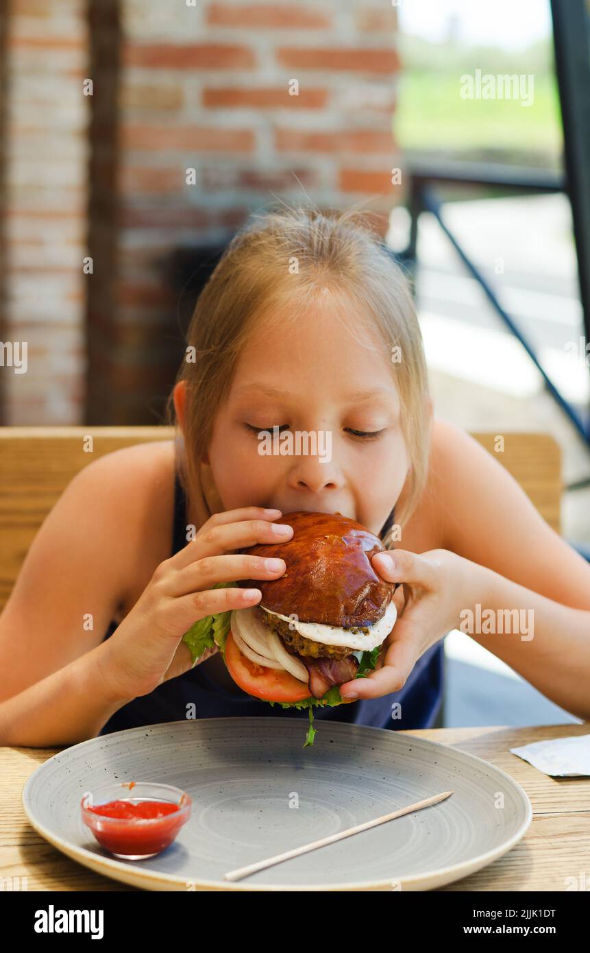Happy girl, teenager eating a burger with a meat patty in a restaurant ...