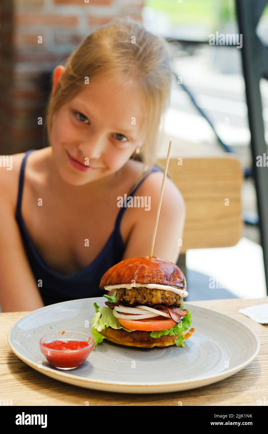 Happy girl, teenager eating a burger with a meat patty in a restaurant ...