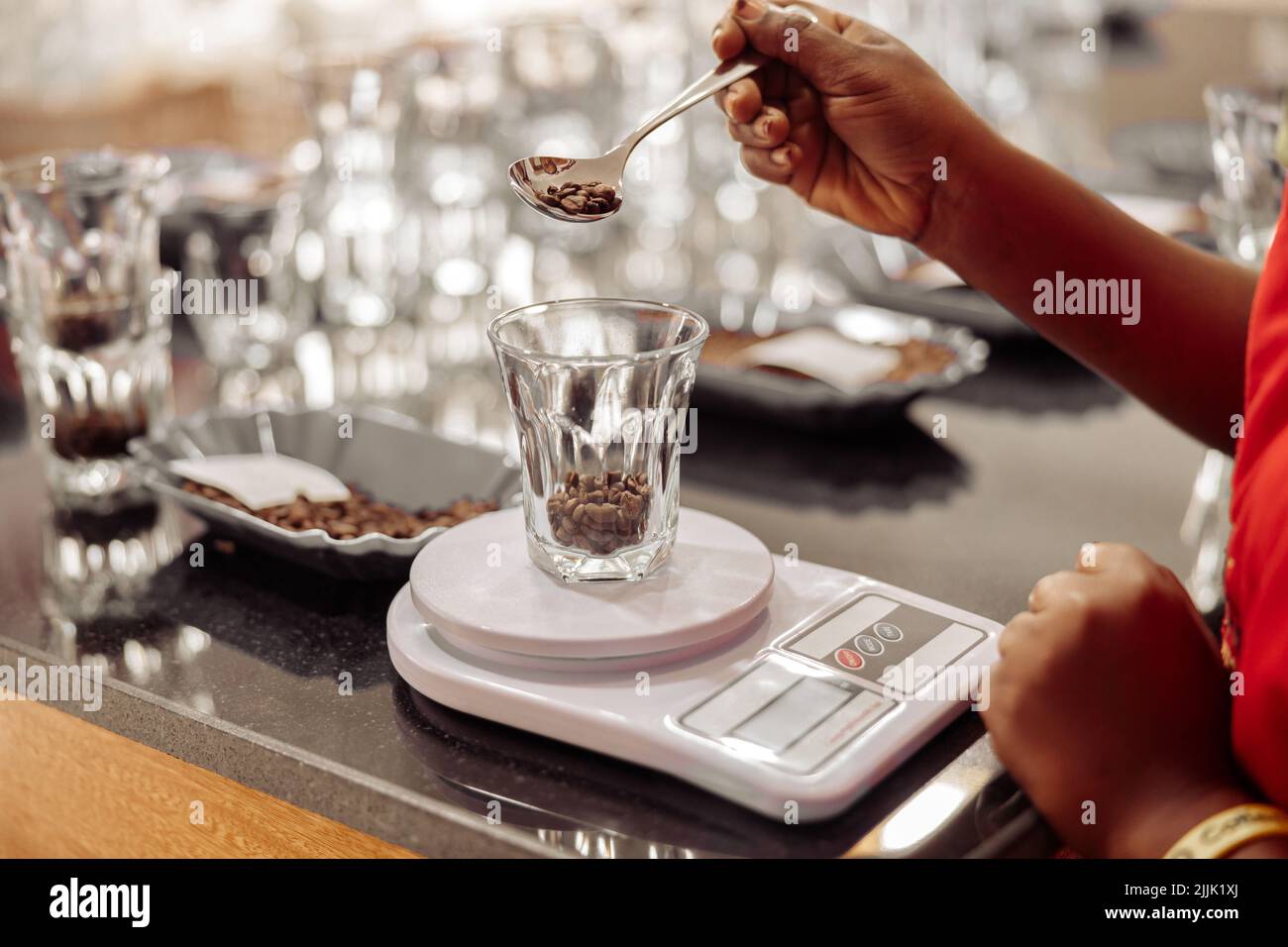 Woman spooning coffee beans into a glass on the scales Stock Photo - Alamy