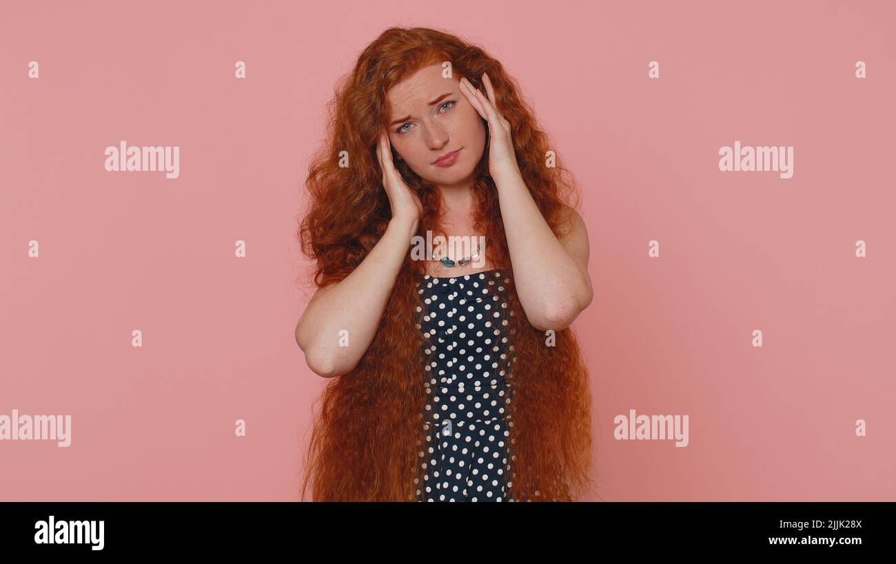 Redhead sleepy young woman in dress rubbing temples to cure headache ...