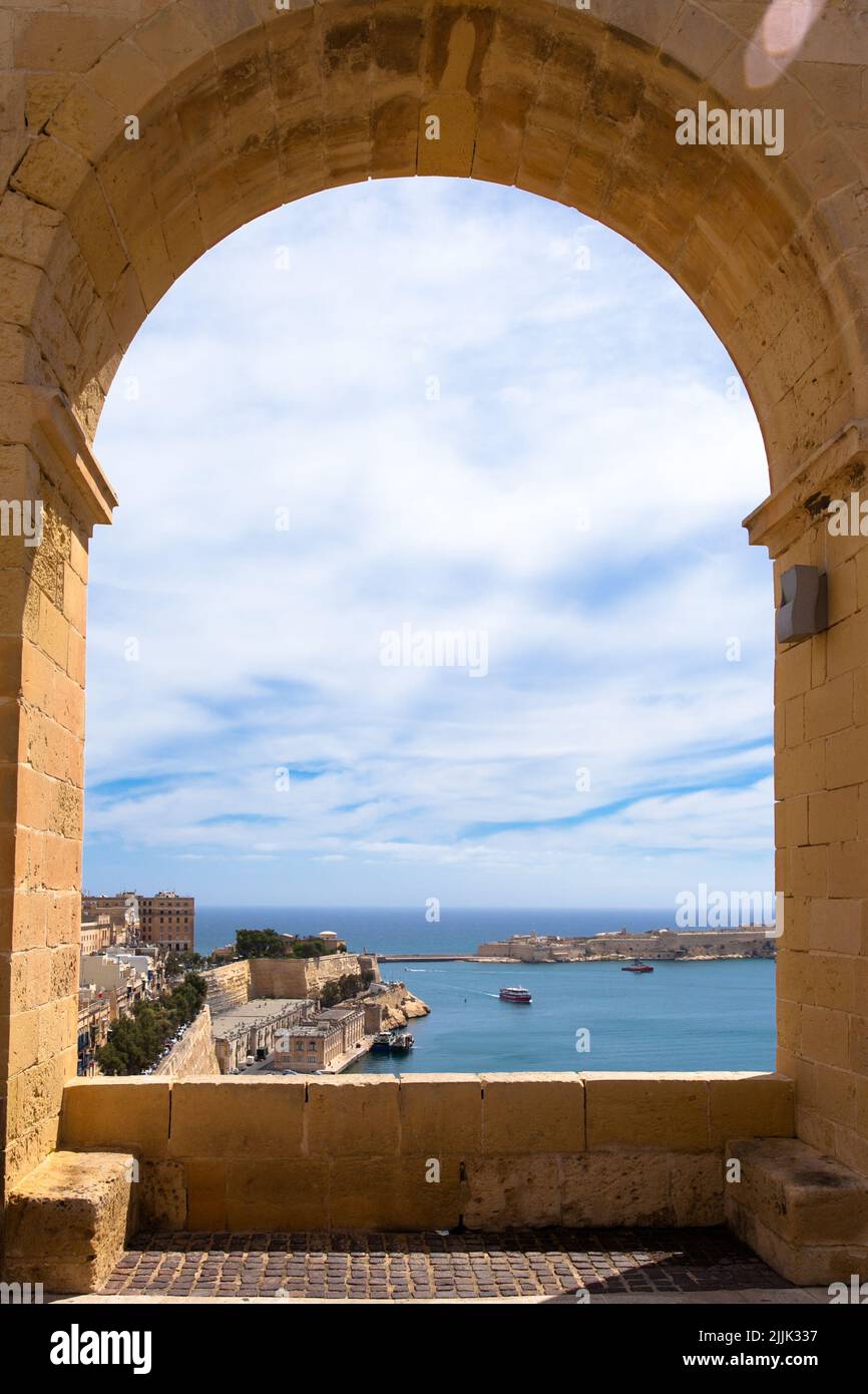 A vertical shot of stony arch with view of sea surrounded by buildings ...