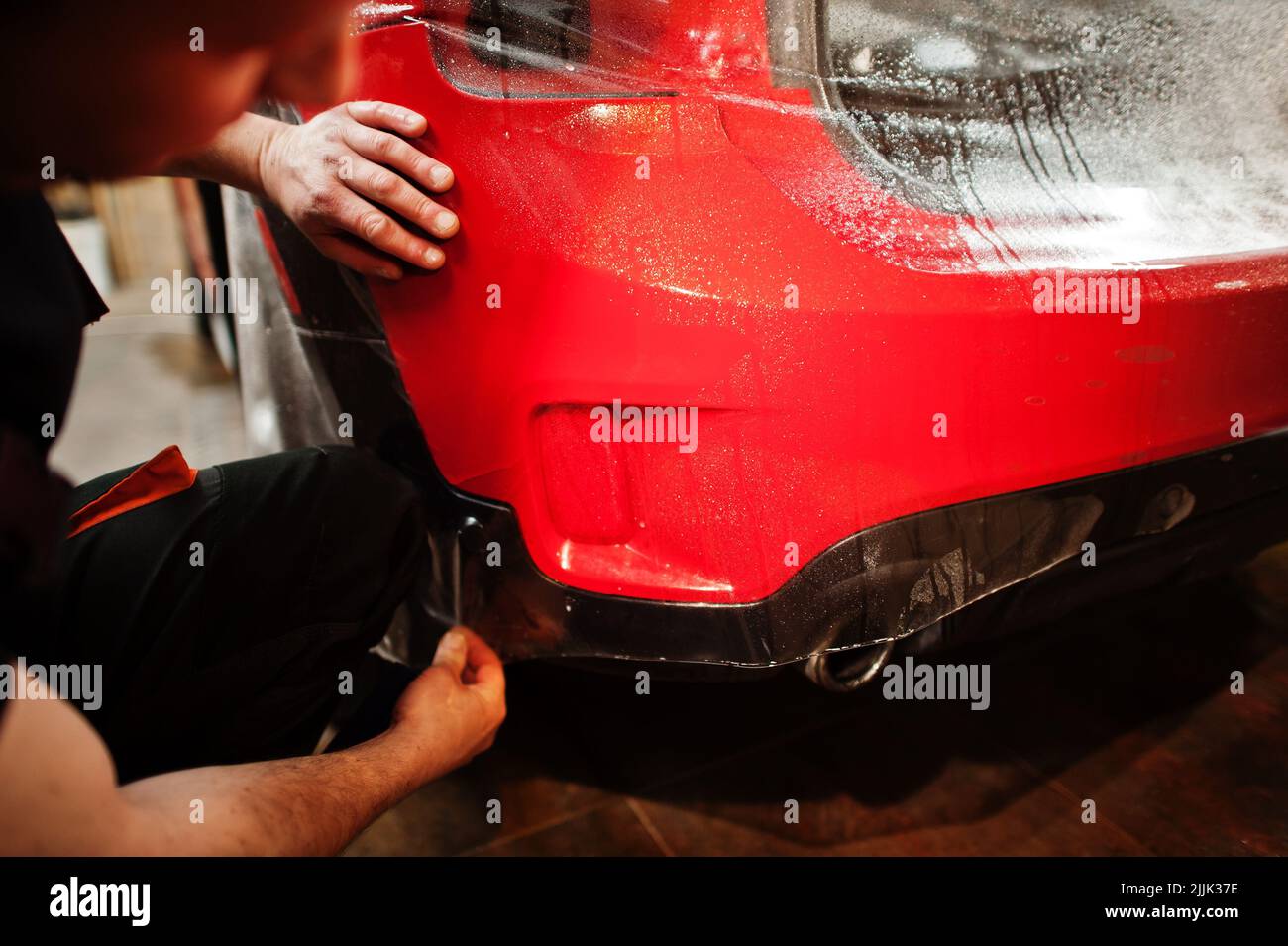 Car service worker put anti gravel film on a red car body at the ...
