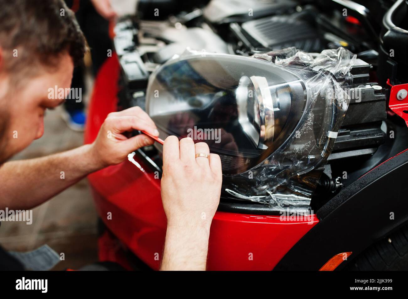 Car service worker put anti gravel film on a red car body at the ...