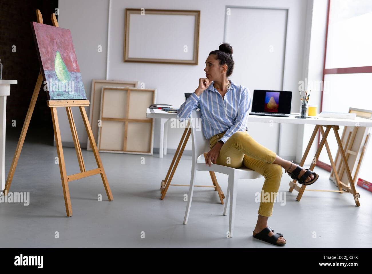 Image of thoughtful biracial female artist sitting on chair in studio ...