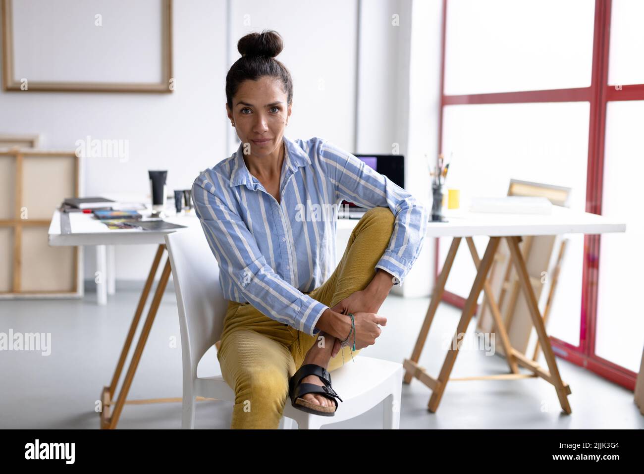 Image of thoughtful biracial female artist sitting on chair in studio ...