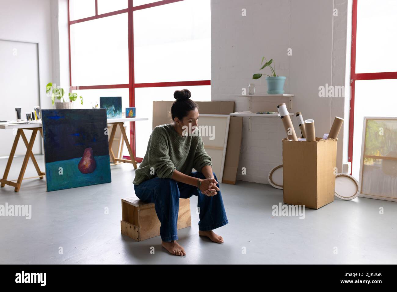 Image of thoughtful biracial female artist sitting in studio Stock ...