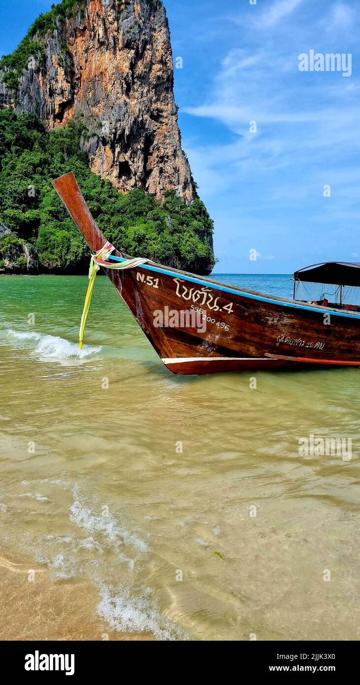 A vertical shot of Bamboo boat floating in water in background of cliff ...