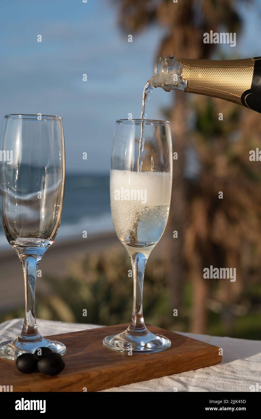 Pouring of Spanish cava sparkling wine is glasses with view on blue sea ...