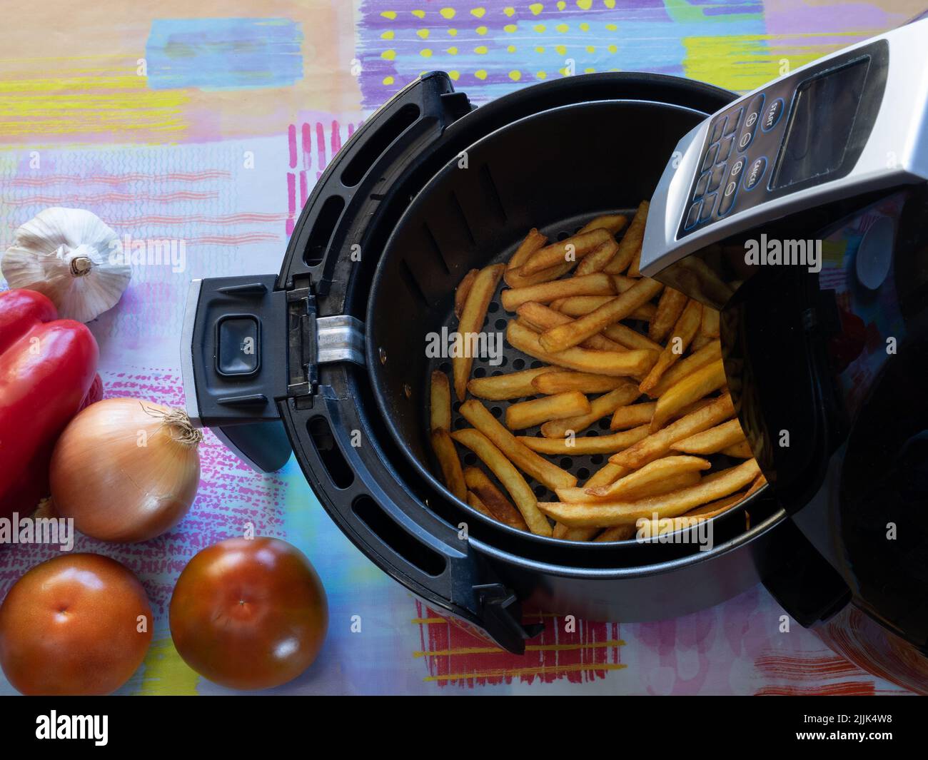 Top view of an air fryer on a table with french fries and vegetables ...