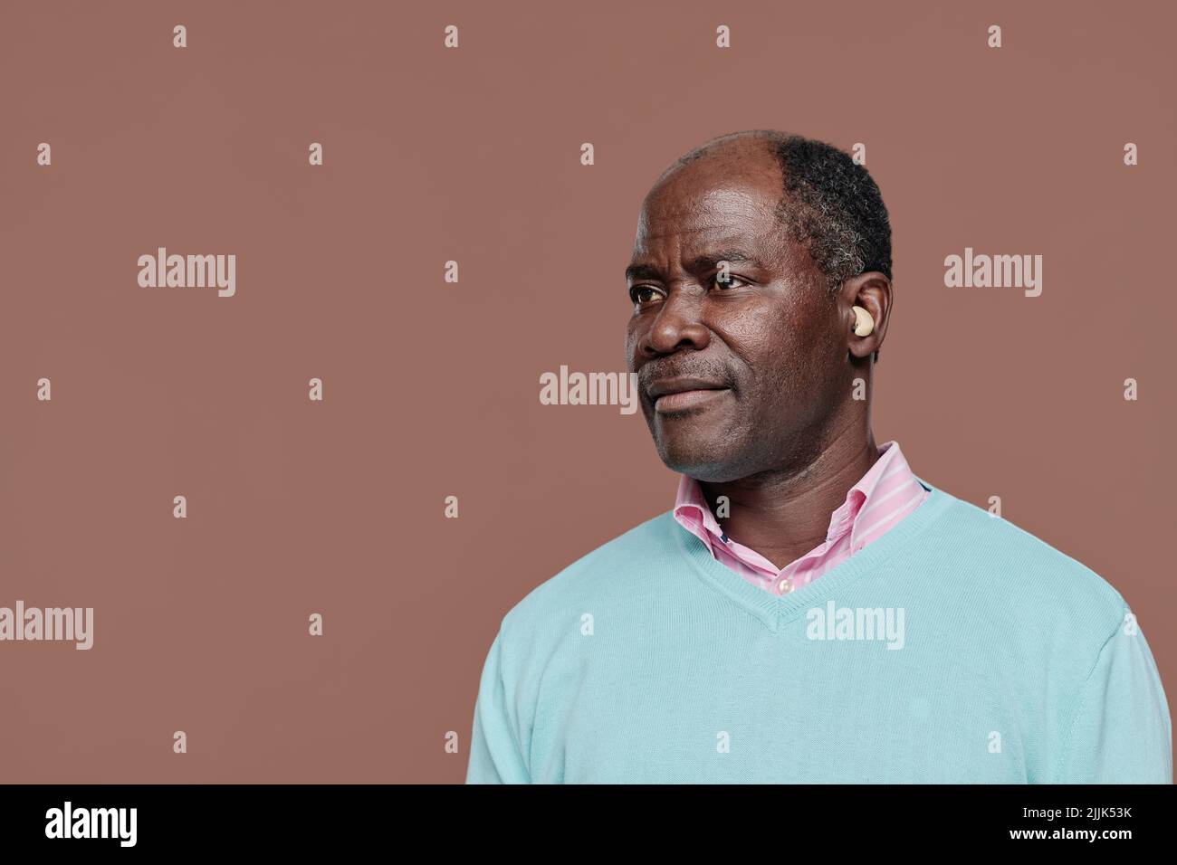 Portrait of senior deaf African man with hearing aid standing against ...