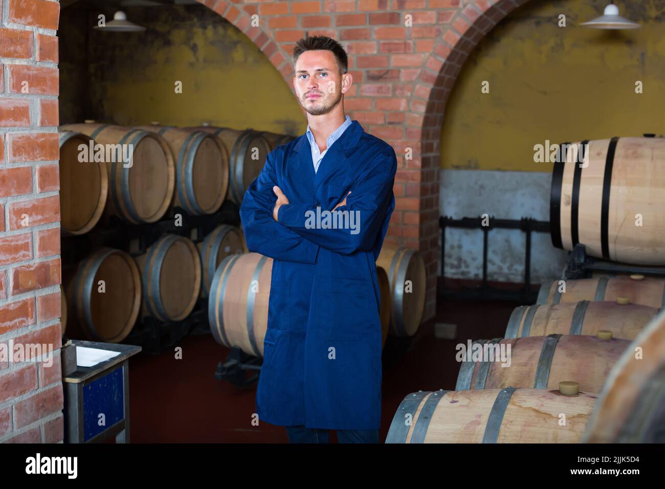Young man wearing uniform standing in cellar with wine woods Stock ...