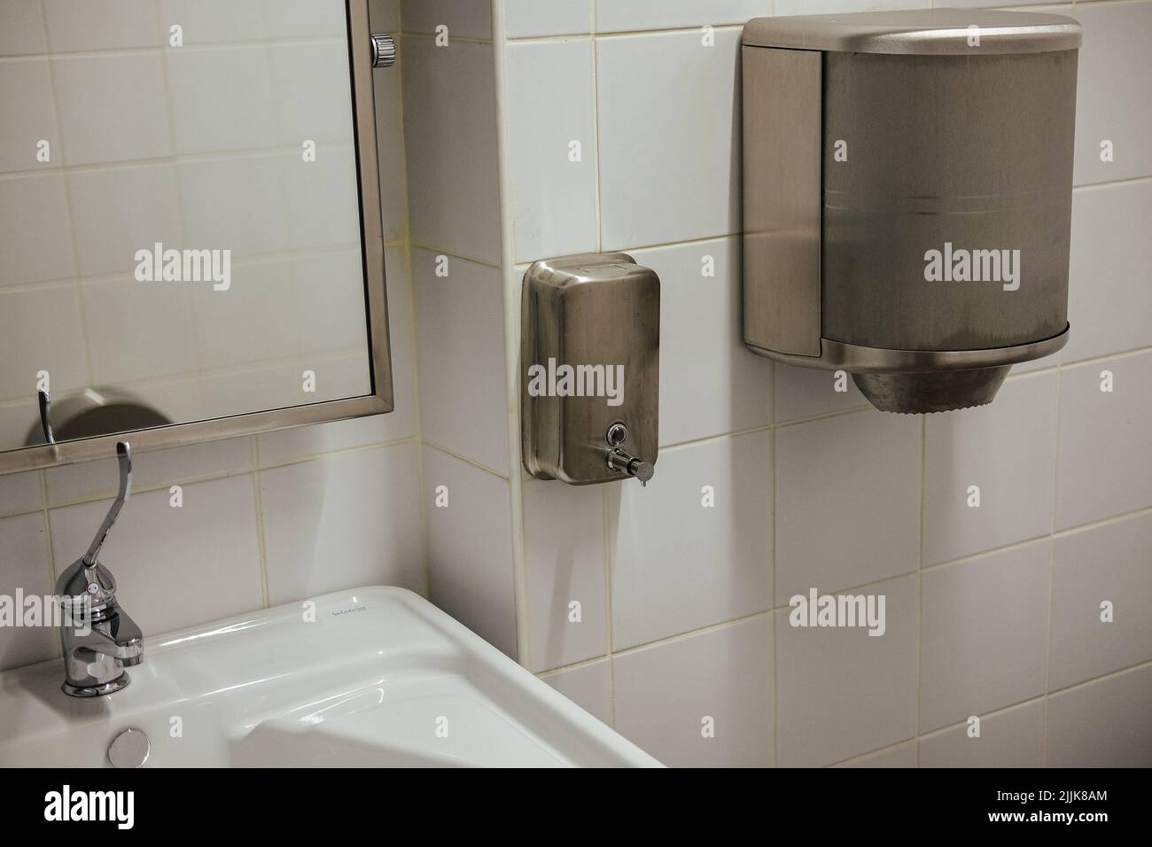 A silver soap dispenser and towel dispenser in a white tile bathroom ...