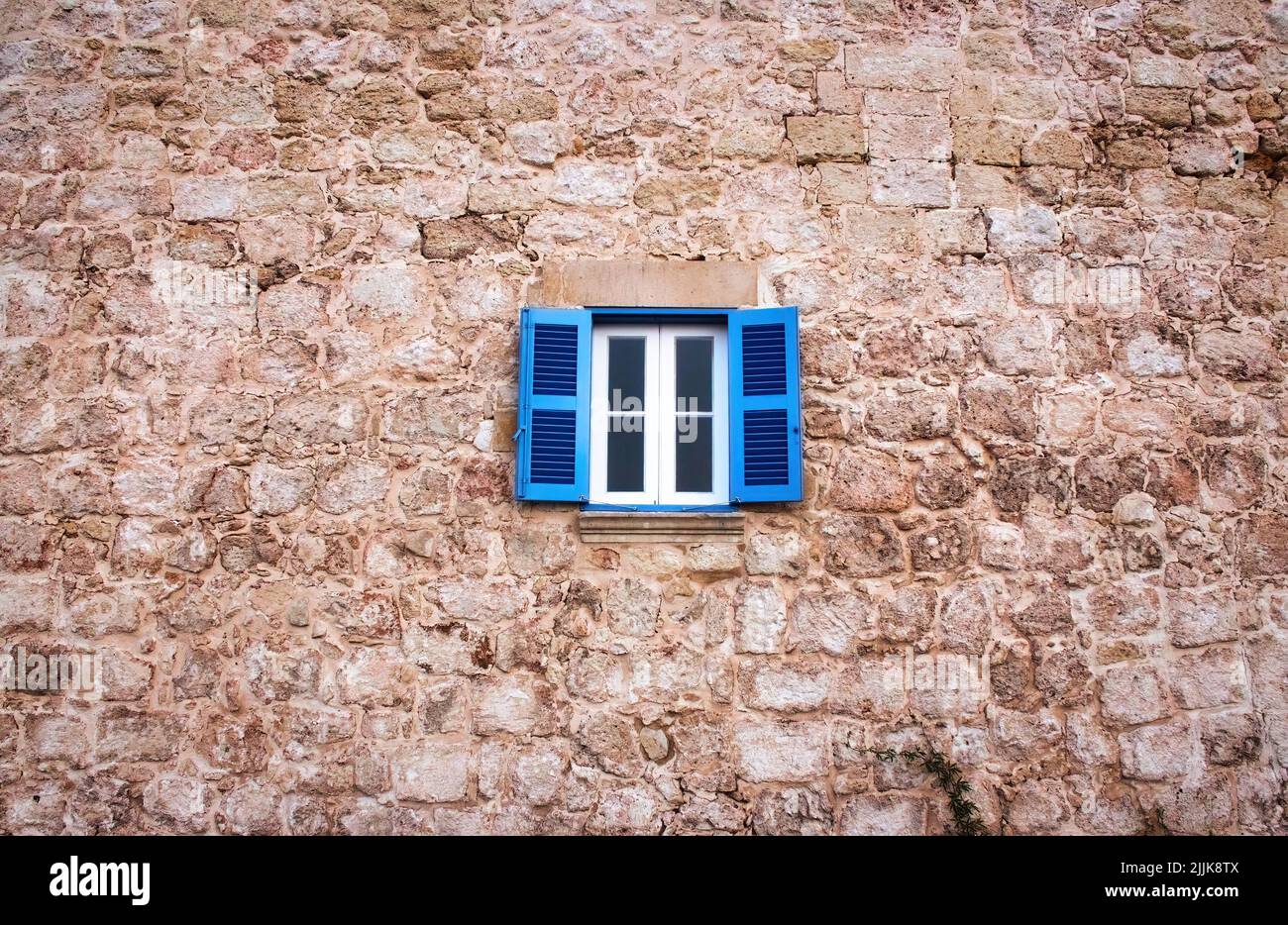 A window with white panes and blue wooden slats set in an old rustic ...