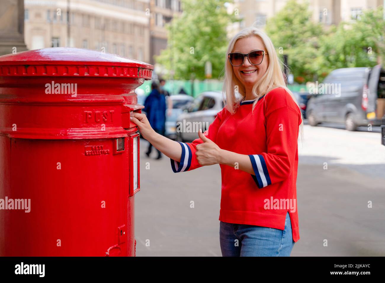 woman in red short posting letters in red post box in England Stock ...
