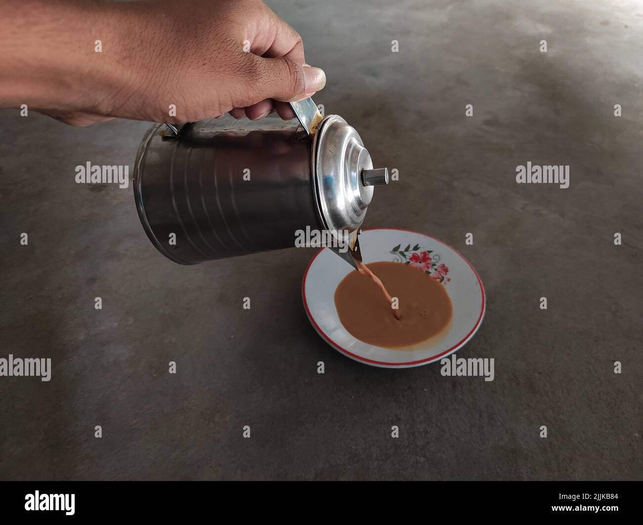 A closeup of a hand pouring Indian village tea from the pot into the ...
