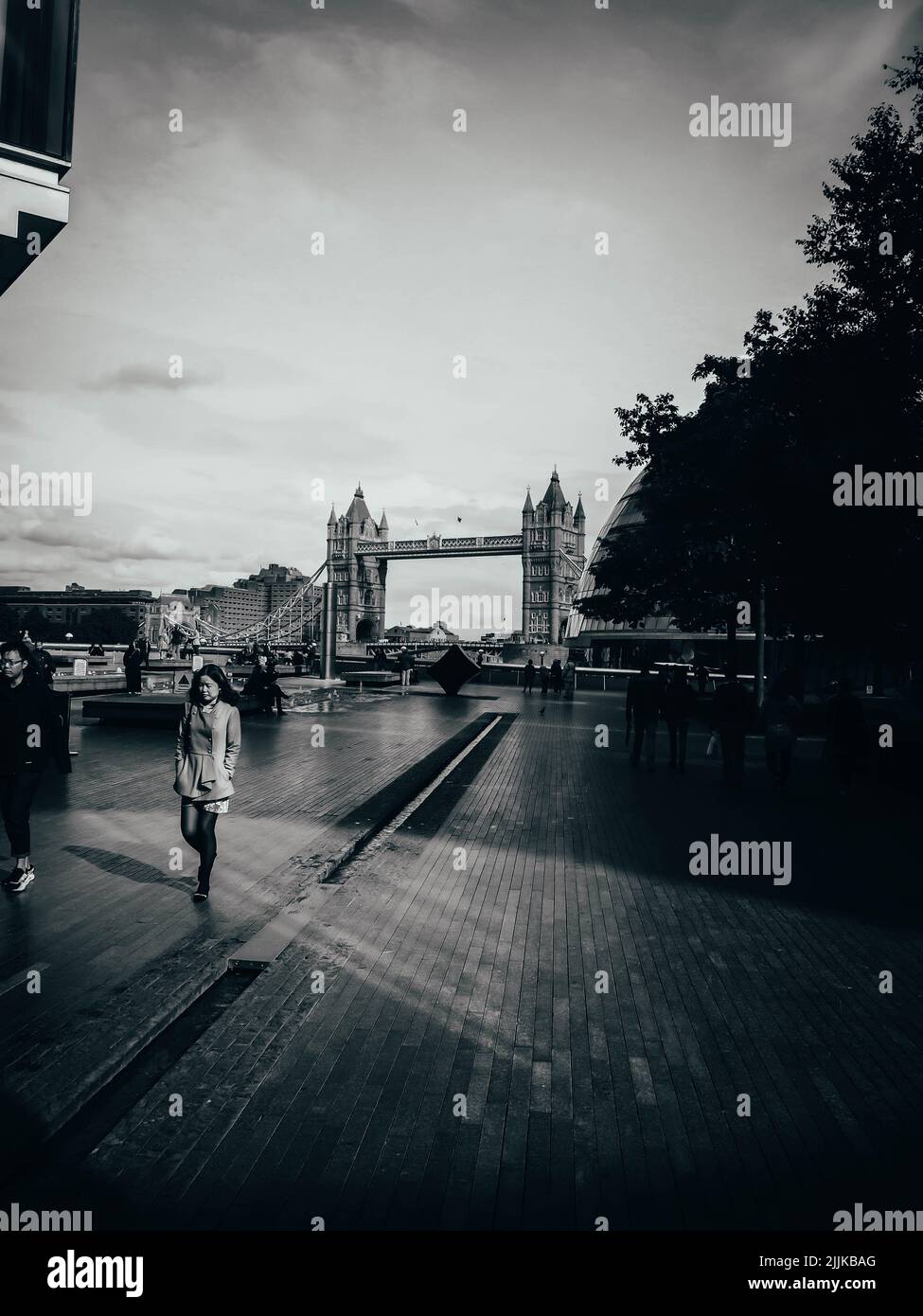 A vertical greyscale photo of a young woman near the Tower Bridge in ...