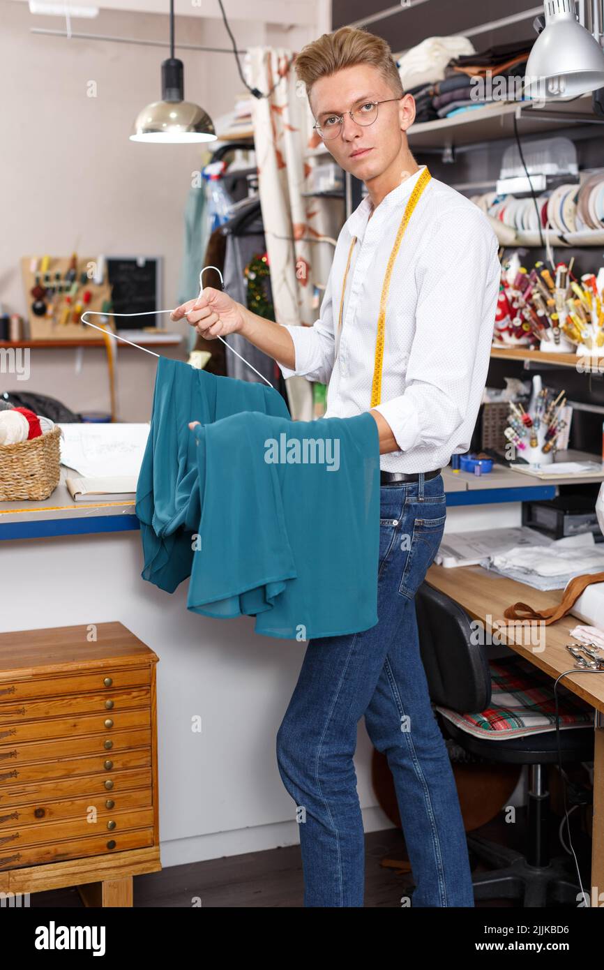 Tailor holding dress at his workplace Stock Photo - Alamy